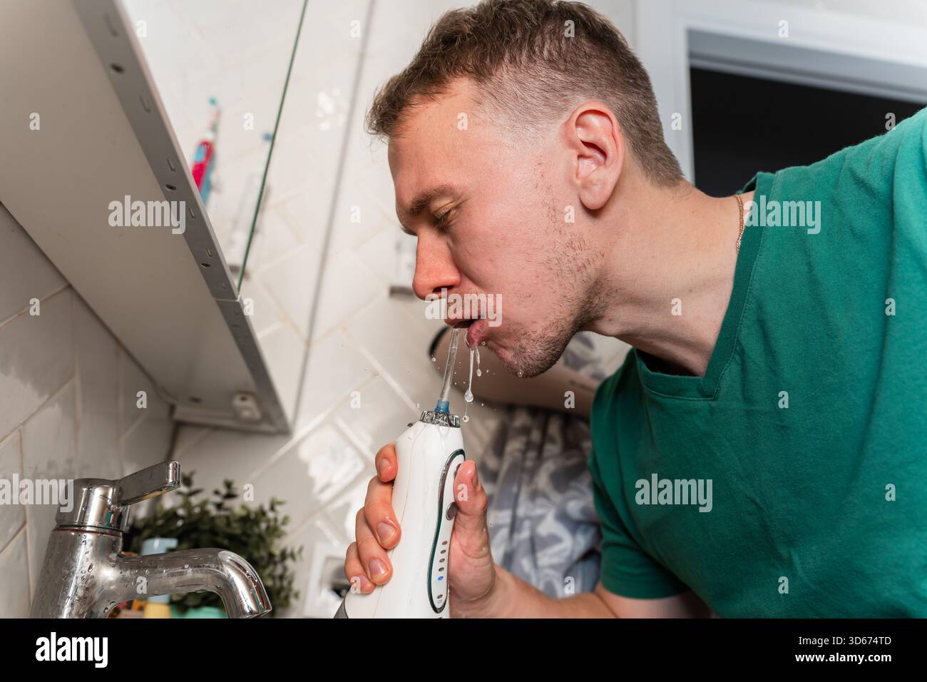 A young man brushes his teeth using an irrigator with a jet of water in ...