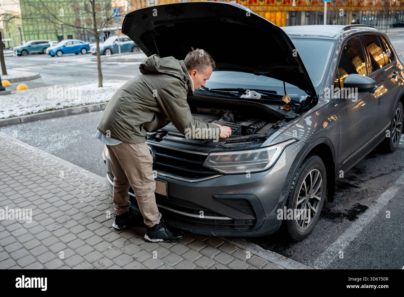 A man is inspecting the engine compartment of a car with the hood open ...