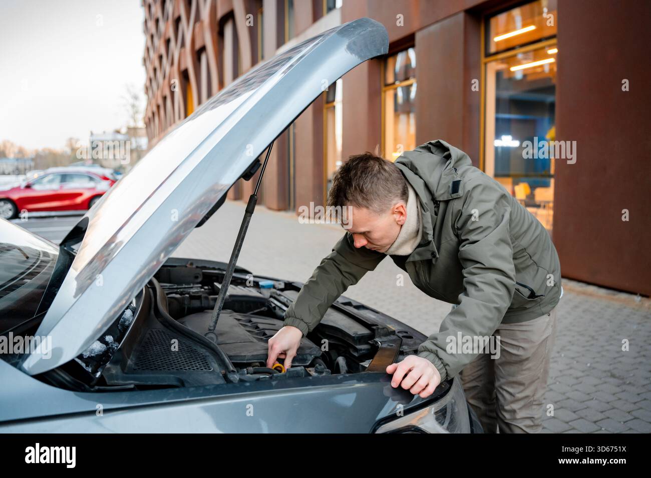 A man is inspecting the engine compartment of a car with the hood open ...