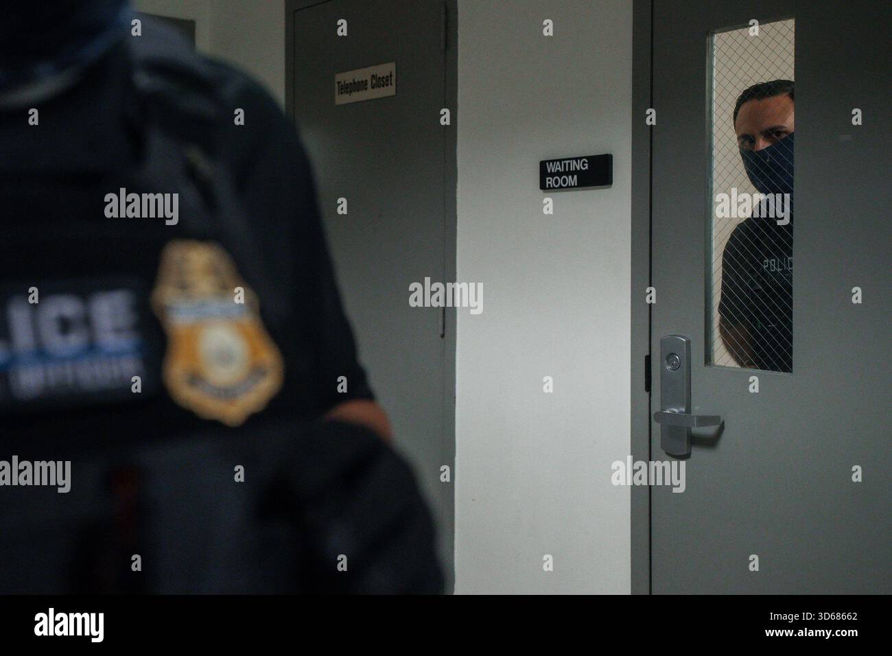 An Immigration and Customs Enforcement agent peers through a door while ...