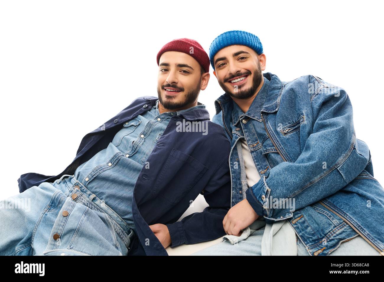 Two twin brothers in trendy outfits smile at the camera while relaxing ...