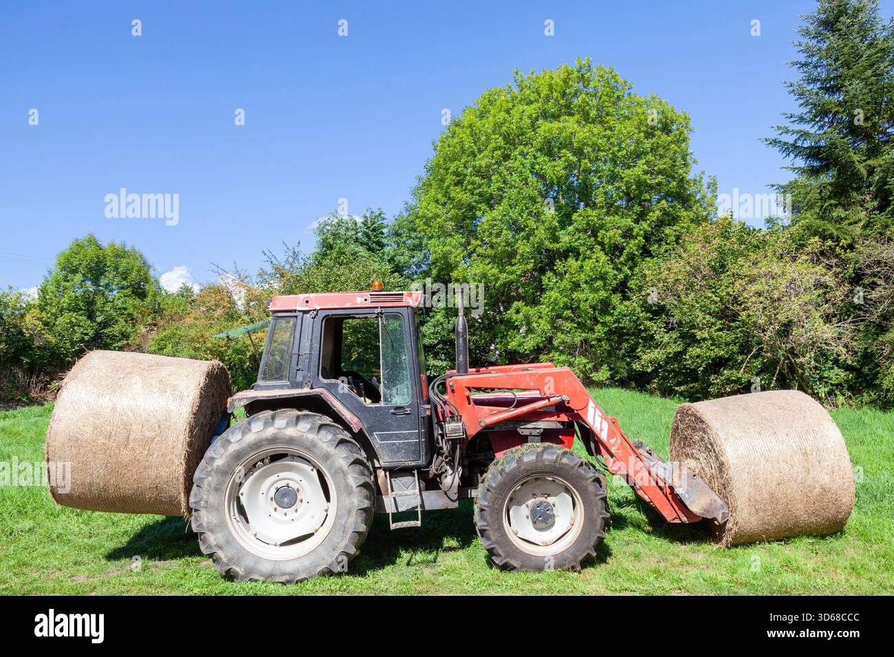 Two circular wheat hay bales being transported on mechanical arms ...