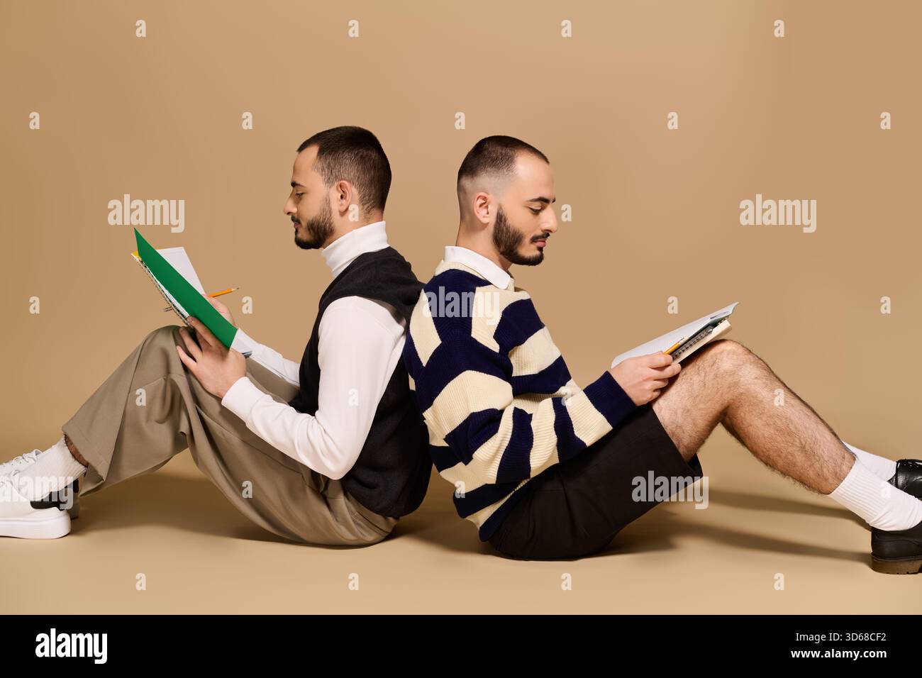 Two fashionable twin brothers sit back to back, deeply engaged in their ...