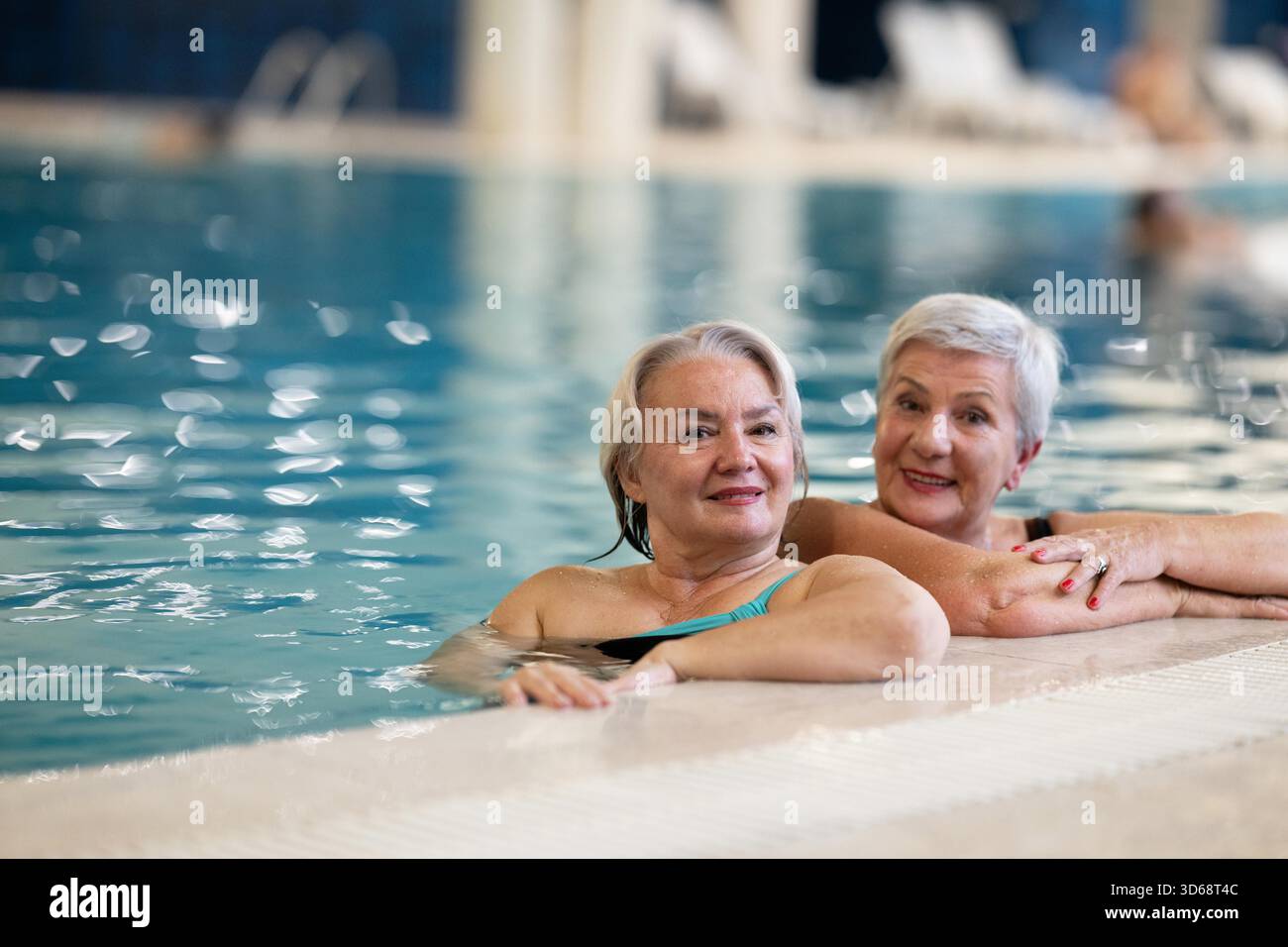 Two smiling senior women enjoying leisure time in an indoor swimming ...