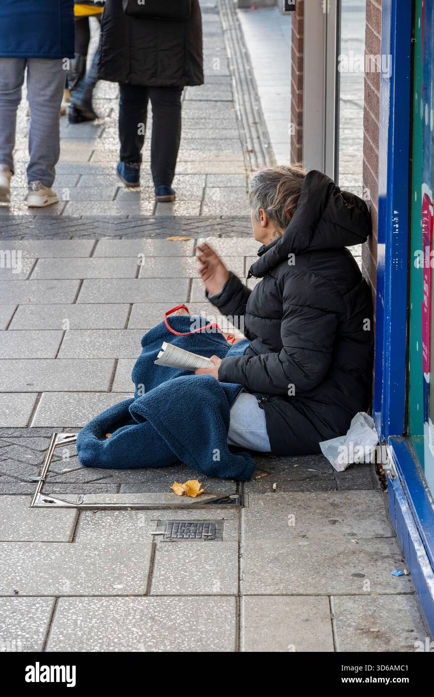 Homeless person sitting on the pavement in a busy town centre begging ...