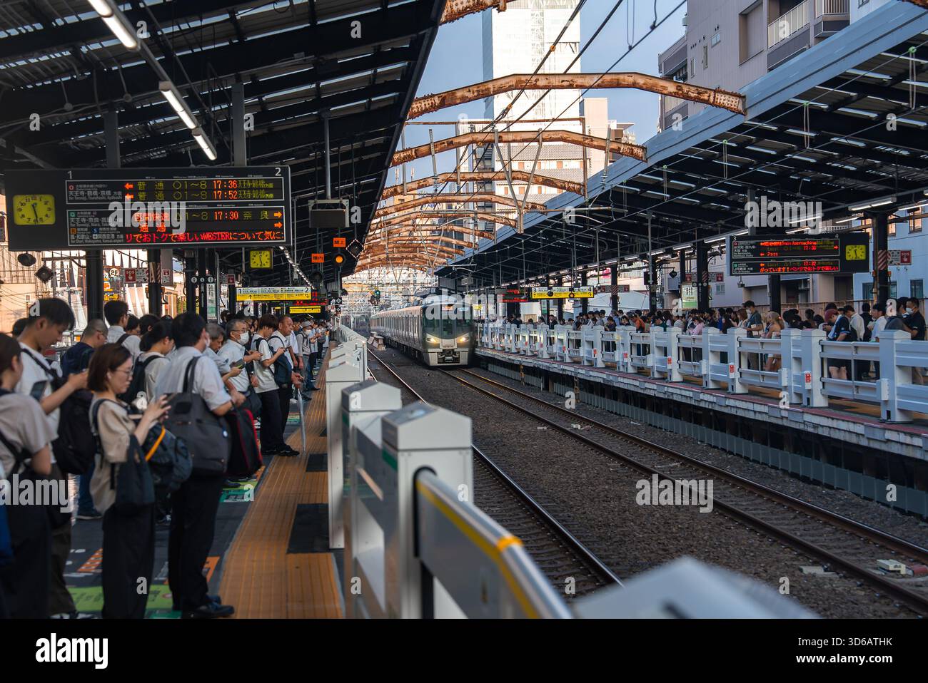 JR train approaches Osaka platform with rush hour queues and signs ...