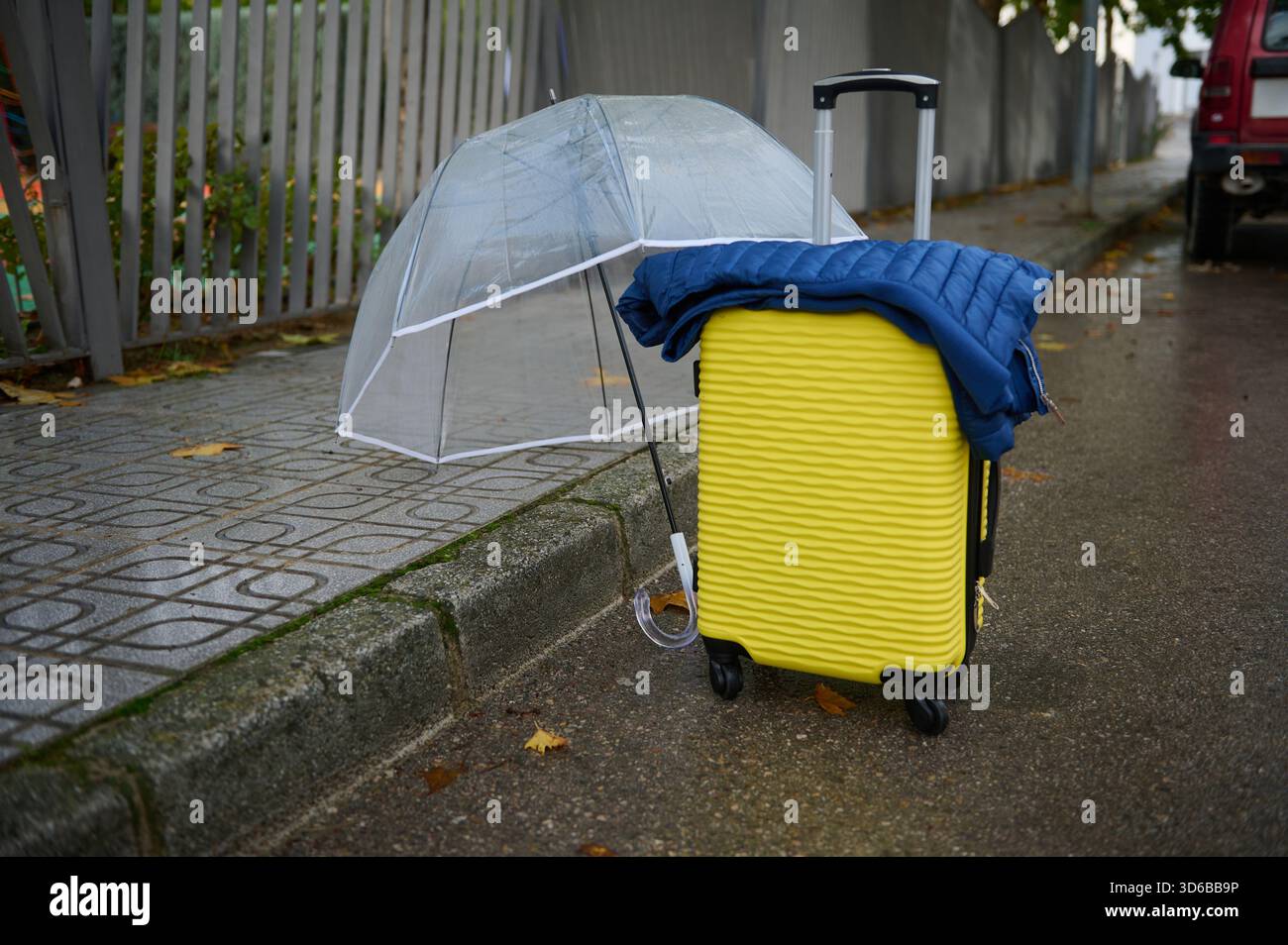 A yellow rolling suitcase with a blue jacket draped over it sits on a ...
