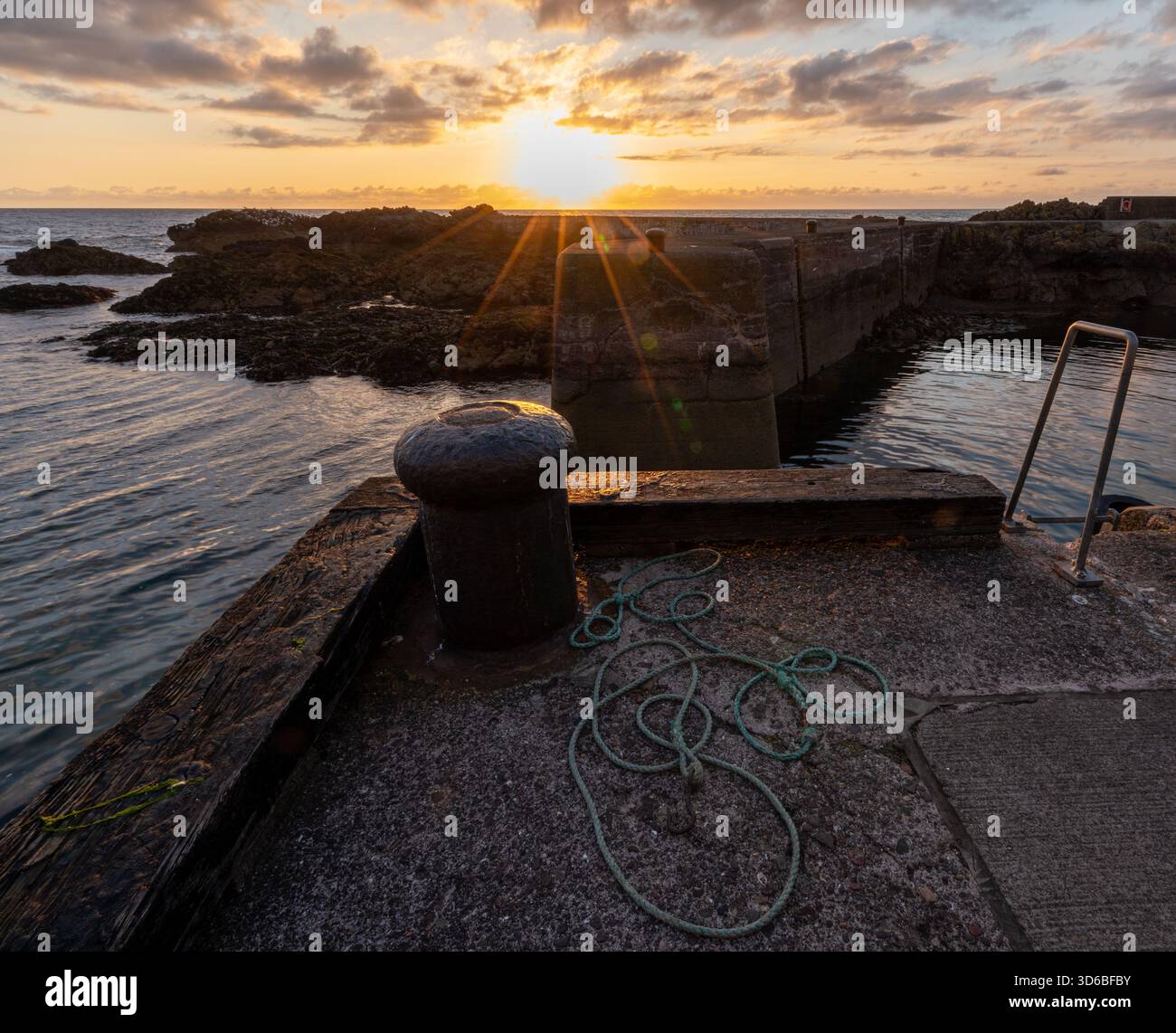 Sunrise light over a harbour pier with mooring bollard, rope and ...