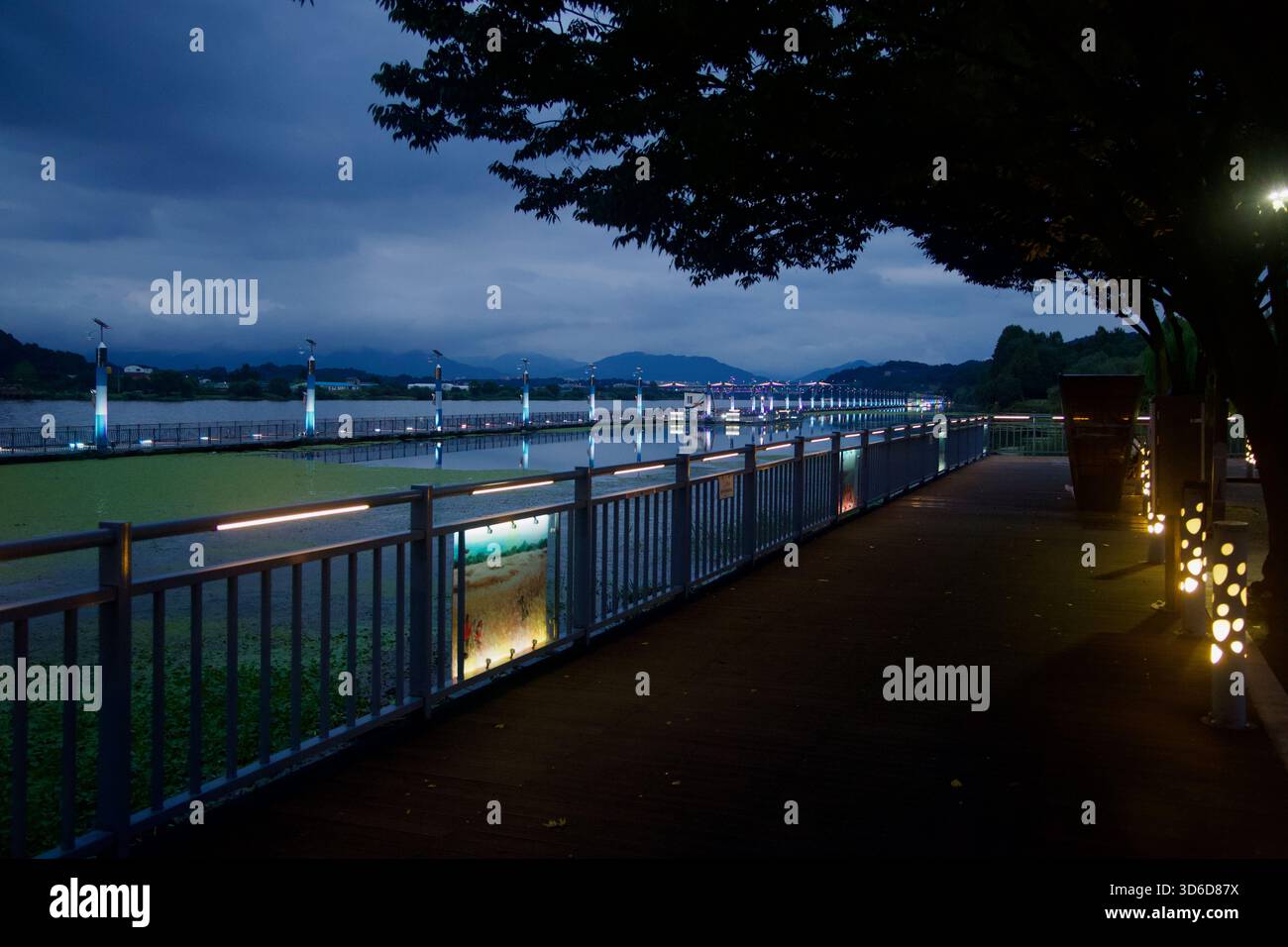 A riverside promenade with railings and lamp bollards parallels the ...
