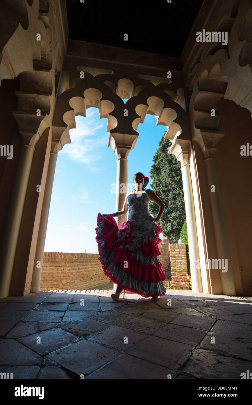 A woman wearing a vibrant flamenco dress poses gracefully in a historic ...