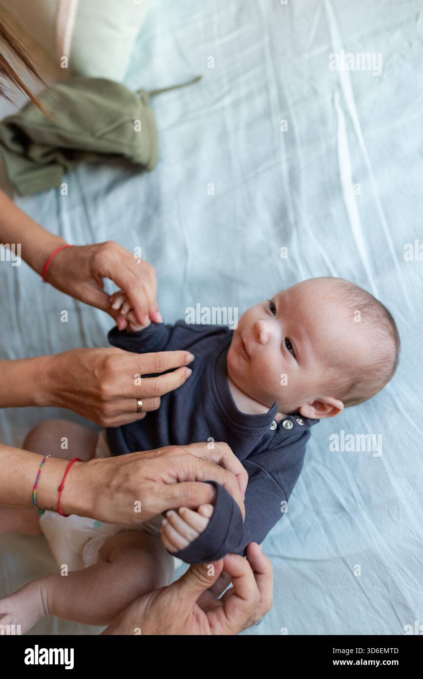 From above of crop unrecognizable parents changing clothes of adorable ...