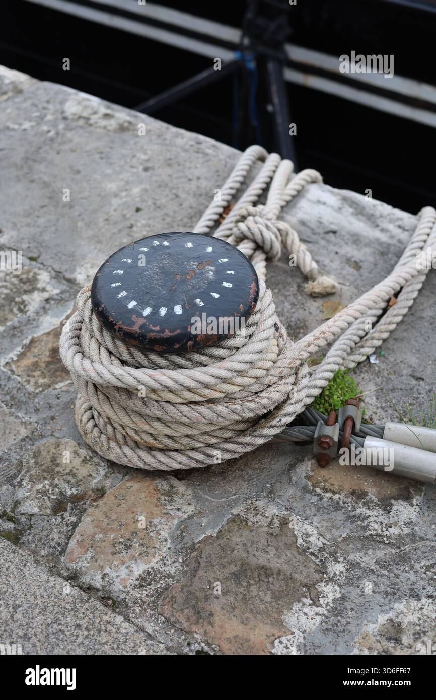 Heavy ropes tied around metal boat mooring bollard to anchor at dock ...