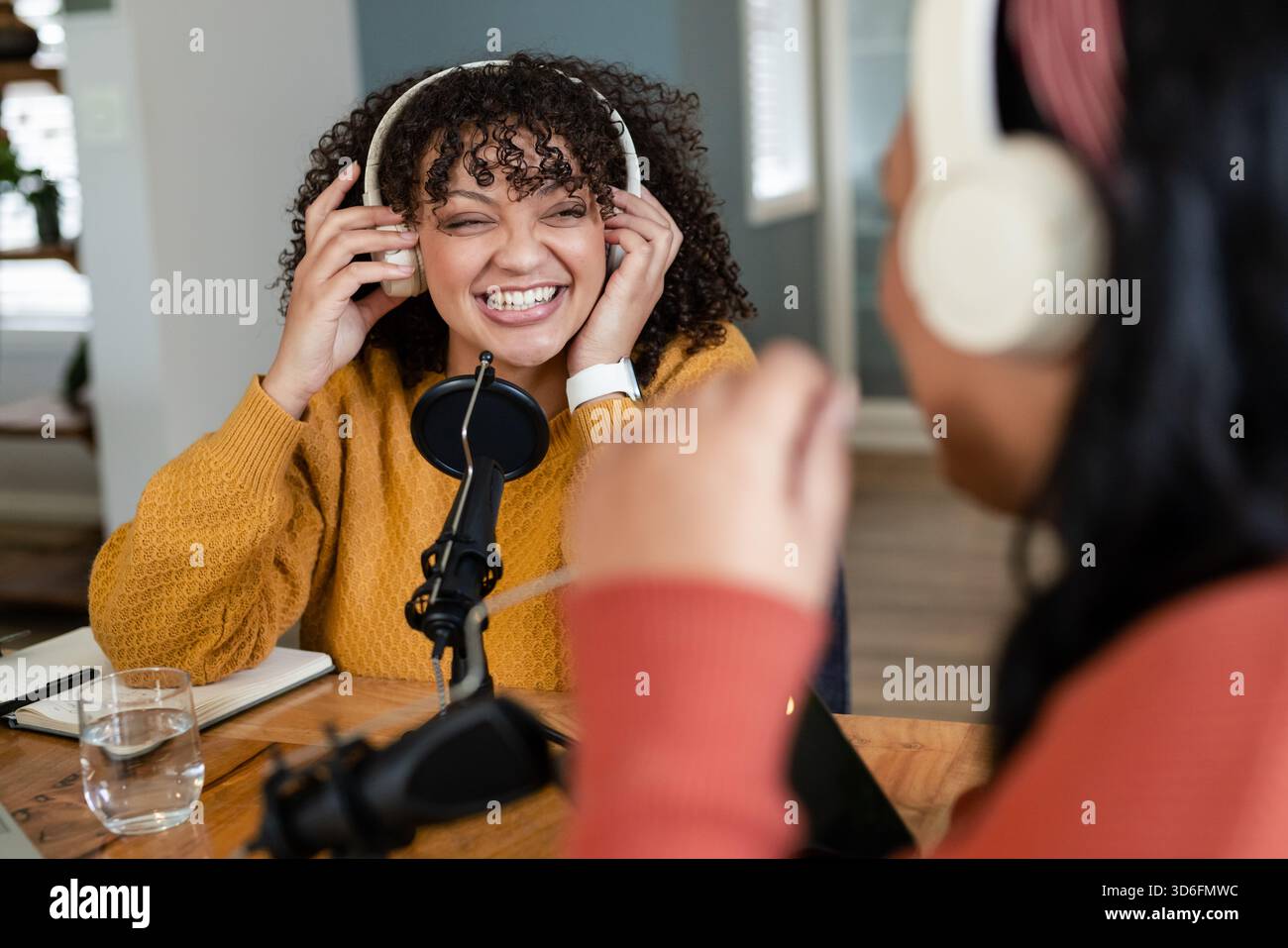 Diverse female co-hosts adjusting over-ear headphones and talking into ...