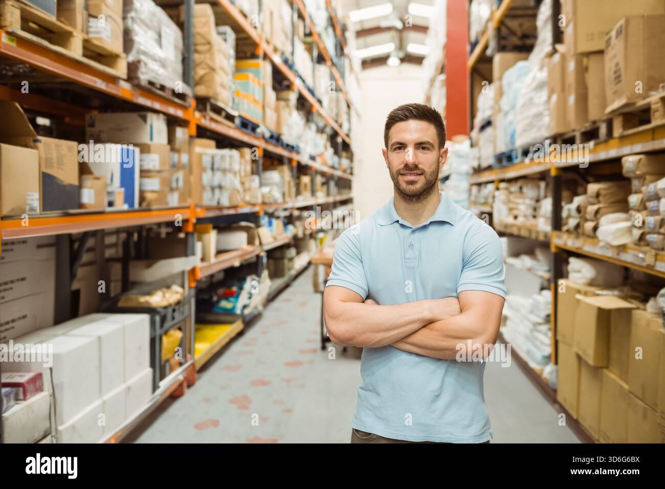 Man in late 20s wearing light blue polo standing in warehouse aisle ...