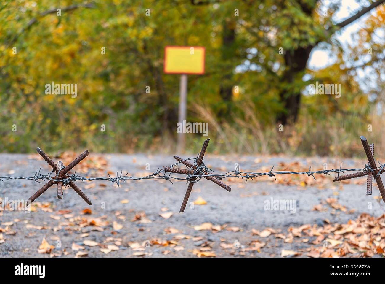 Barbed wire stretches across a dirt path surrounded by fallen leaves ...