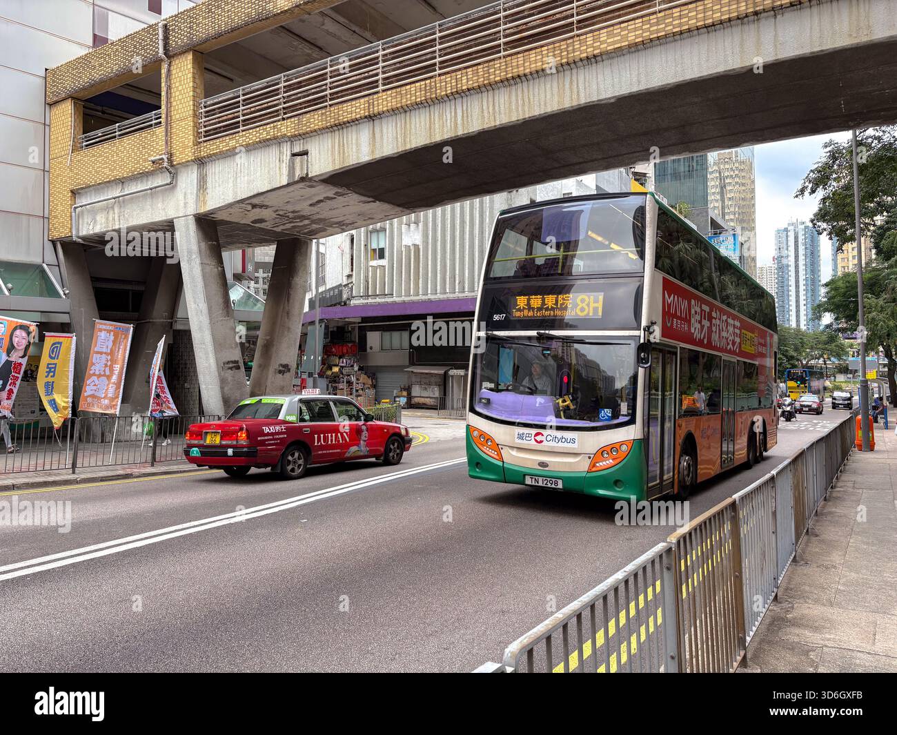 A green and orange Citybus double decker bus drives under a pedestrian ...