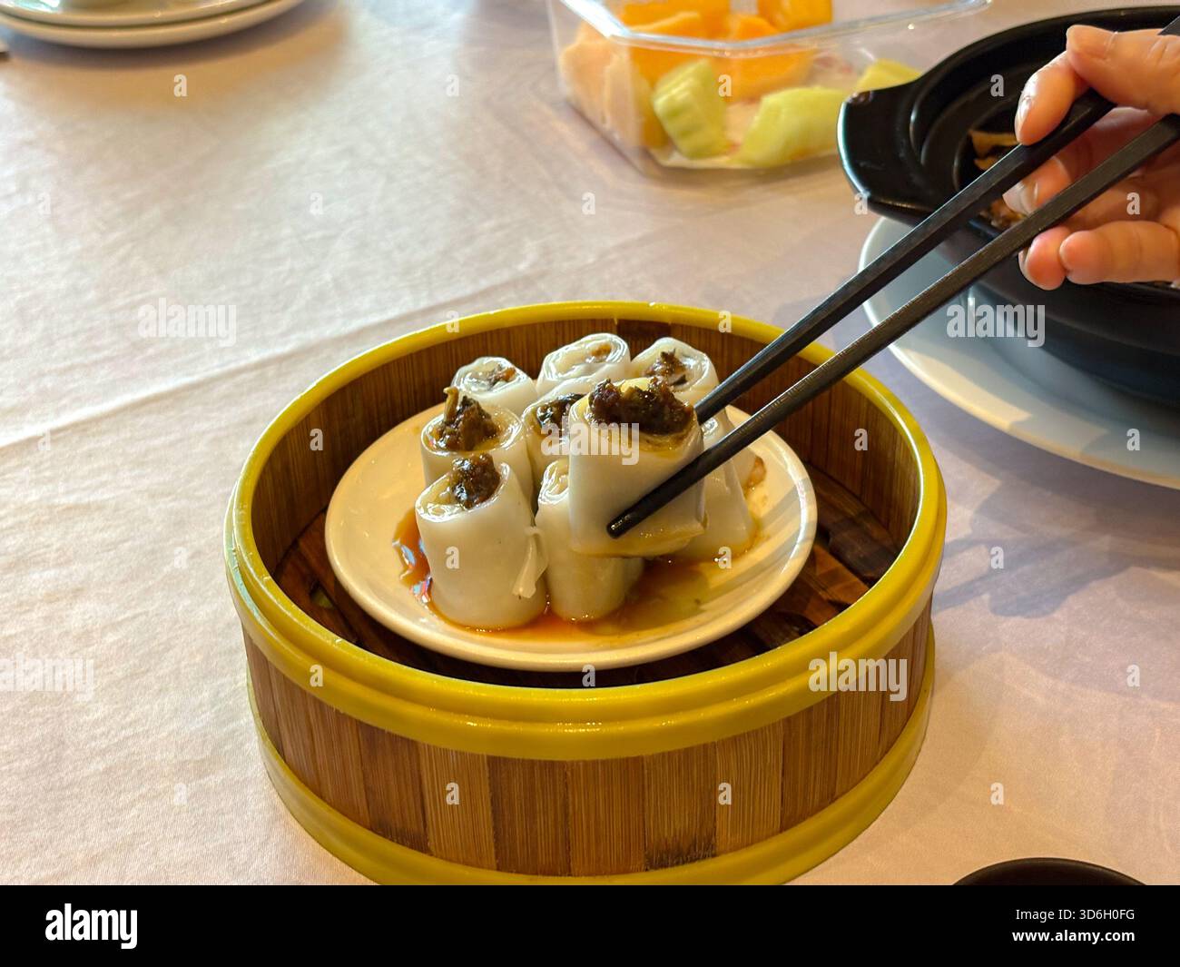 Dim sum. A person picks up a steamed rice roll with savory filling ...
