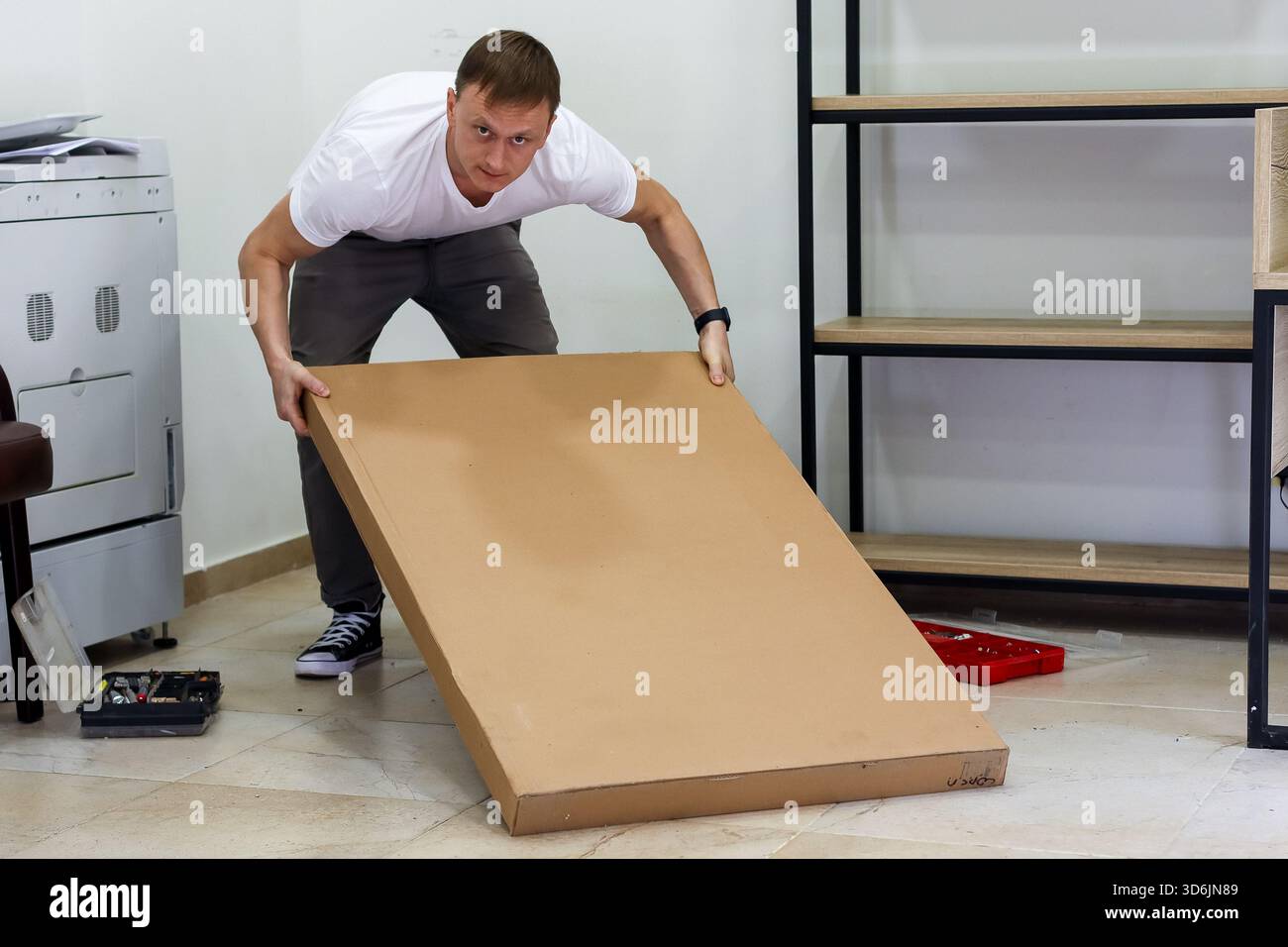 Man bending over to lift large flat cardboard box. Strong man in casual ...
