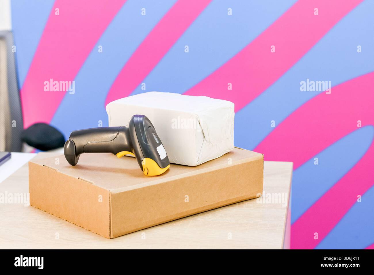 Handheld scanner placed on cardboard beside wrapped parcel on wooden ...