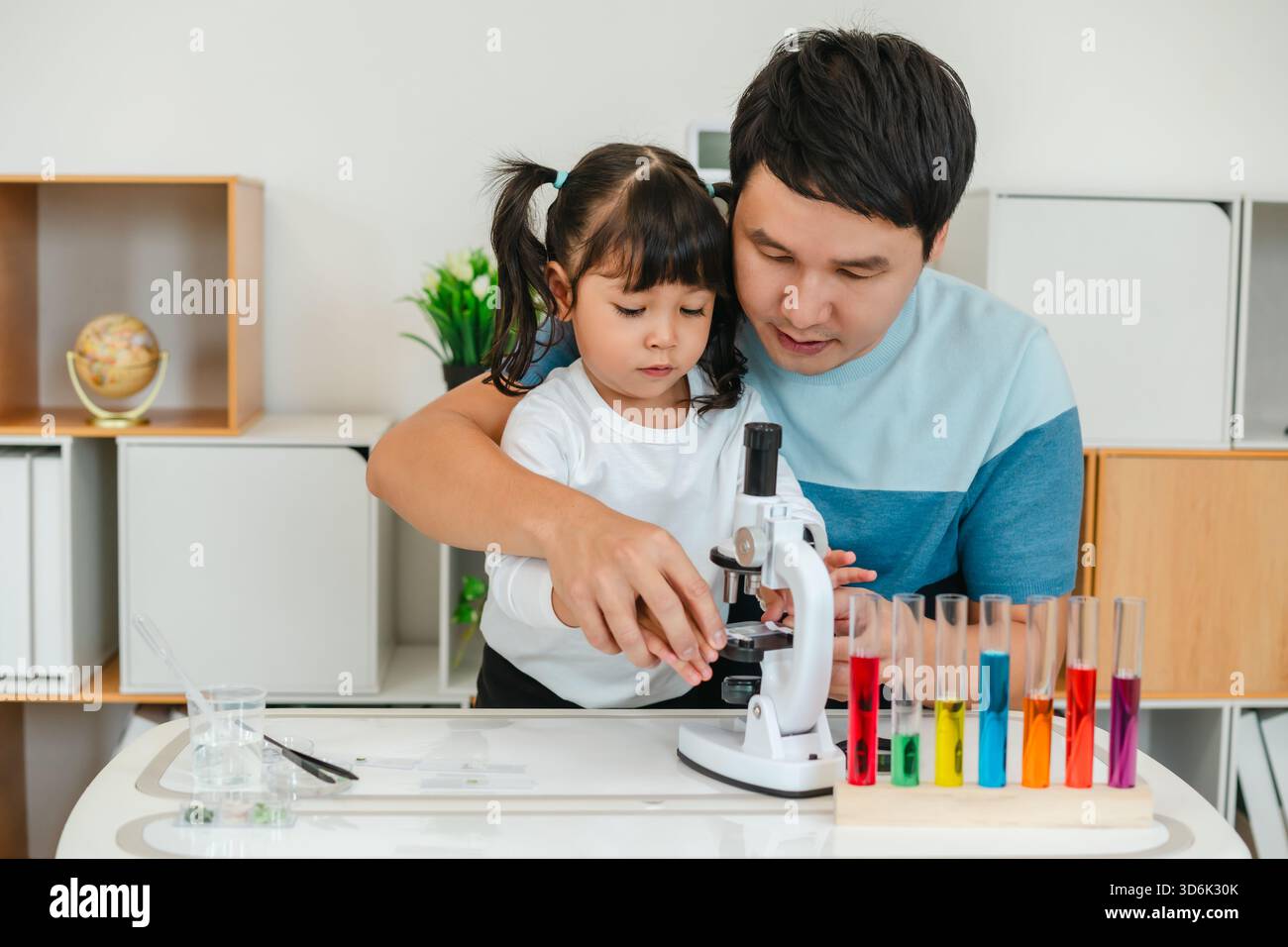 father and toddler girl scientist placing microscope slides with ...