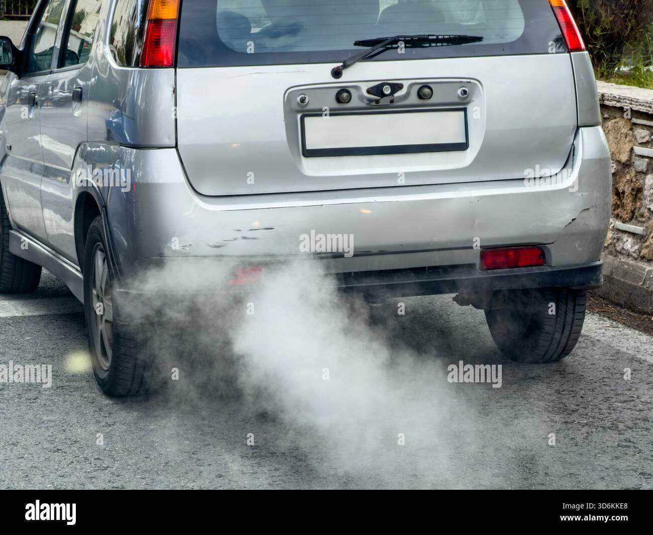 Old silver car releasing thick exhaust smoke on city street, daytime ...