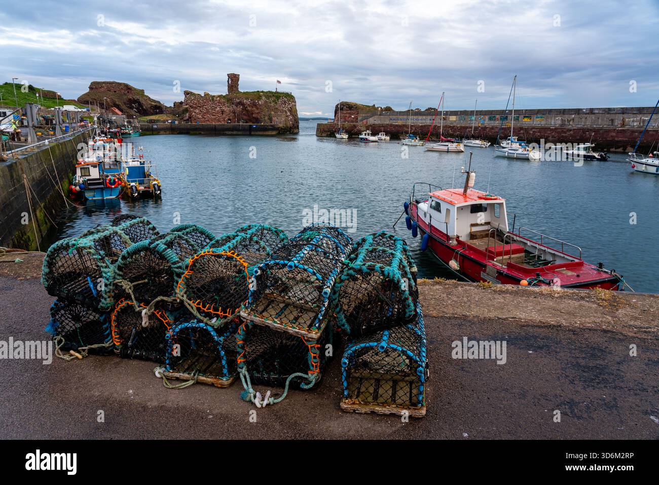 Lobster pots and fishing boats at Dunbar harbour with the ruined Dunbar ...