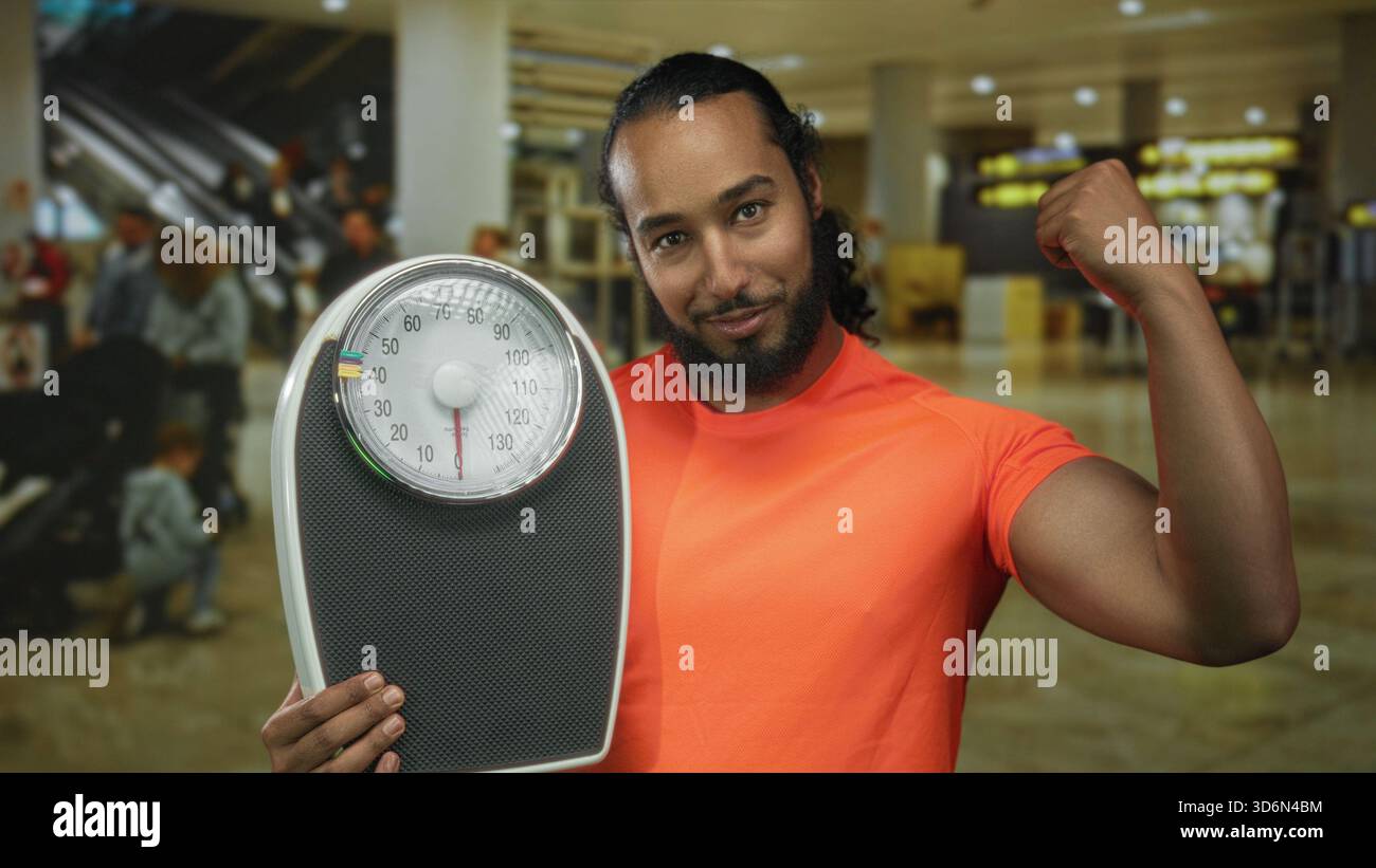 Man holding bathroom scale with visible dial flexes bicep and points to ...