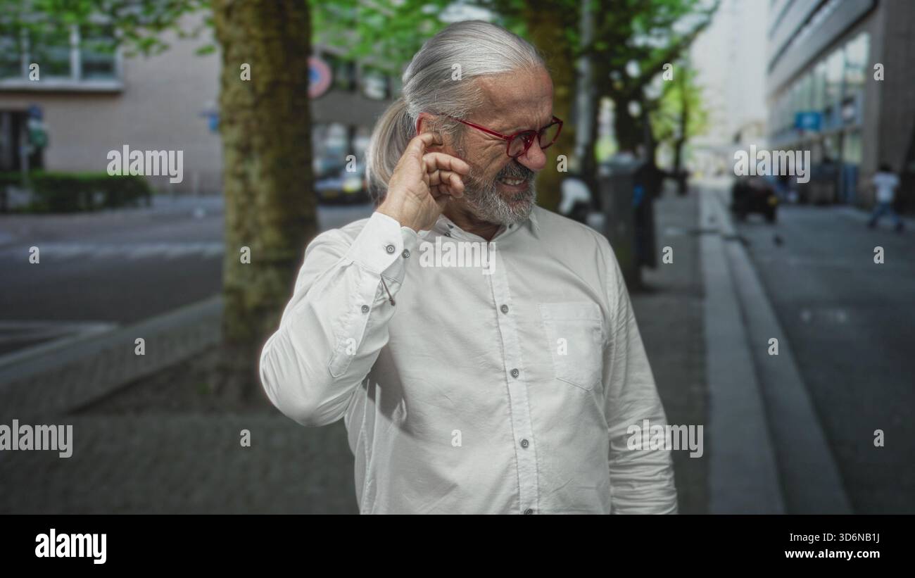 Man pressing hands to ears on a busy street near a tree and storefronts ...
