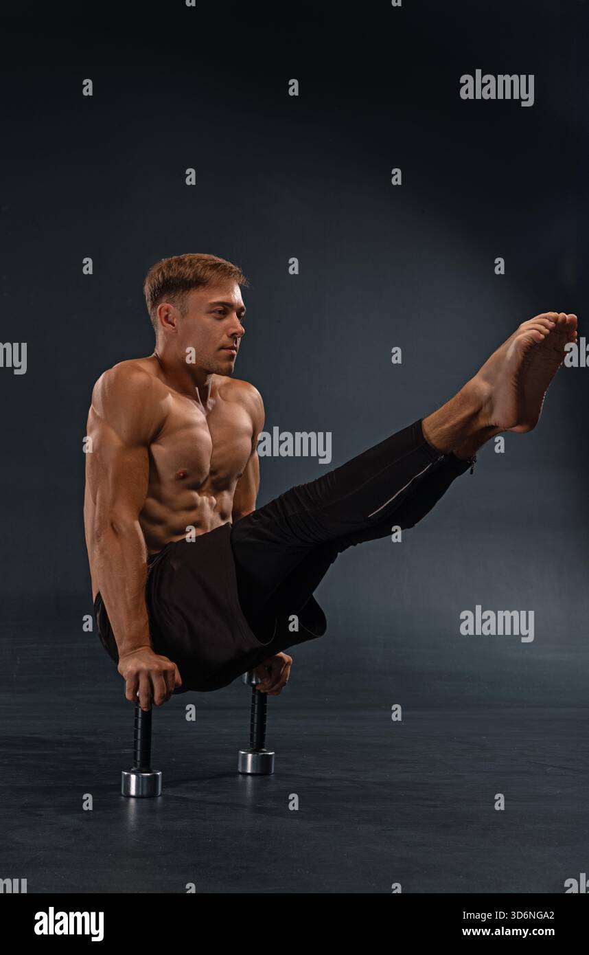 muscular man is executing a challenging leg lift on parallel bars in a ...