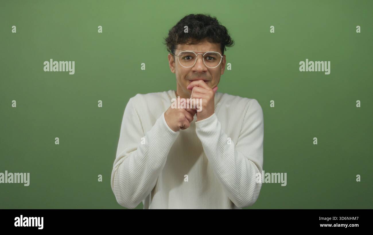 Young hispanic man biting fingernails with tense face in green studio ...