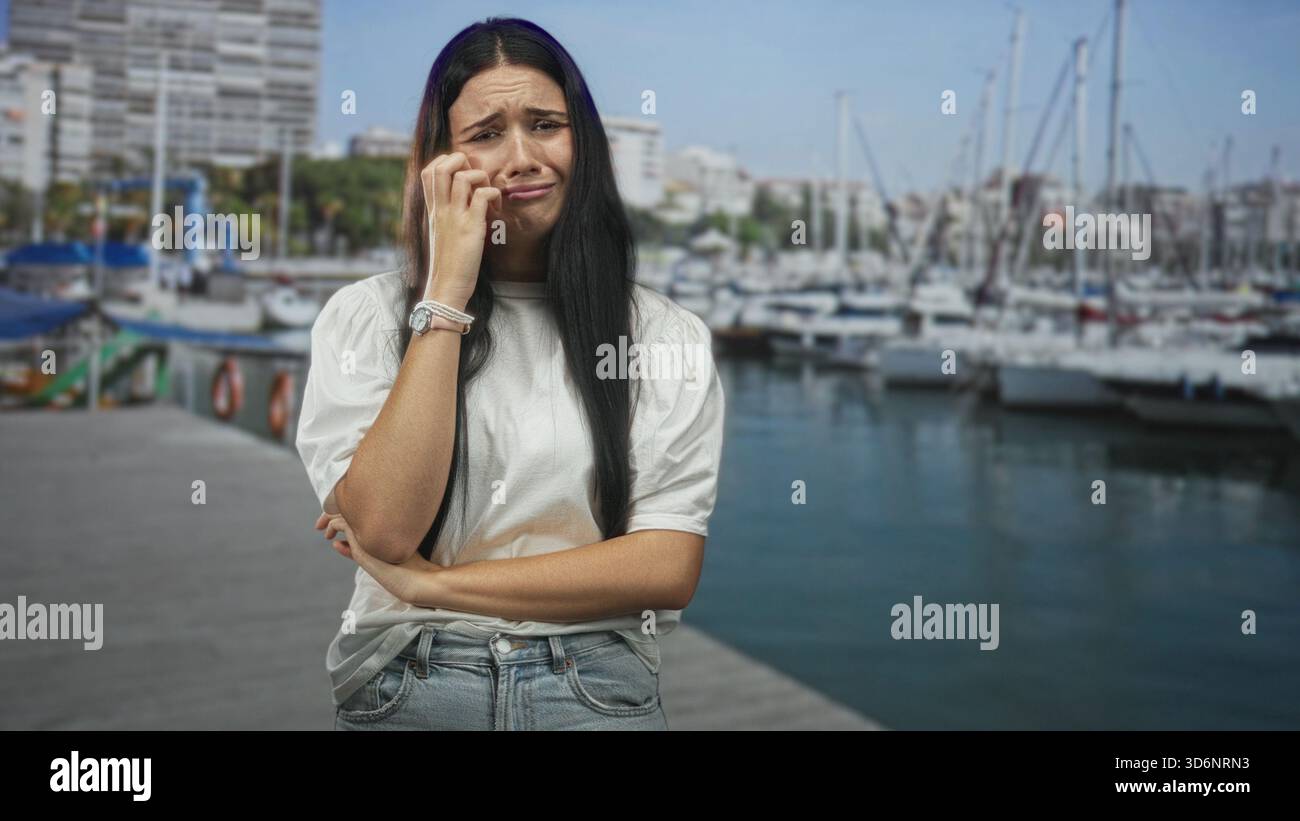 Woman wiping tears with hand on face and crossed arm on chest at marina ...