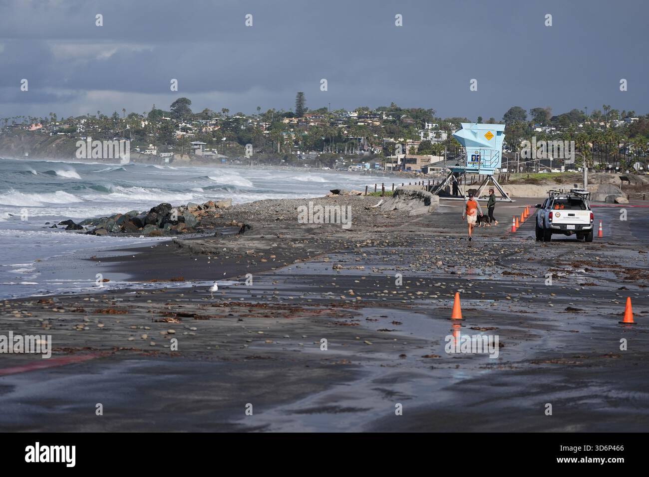 People make their way past a walkway and parking lot eroded by a ...