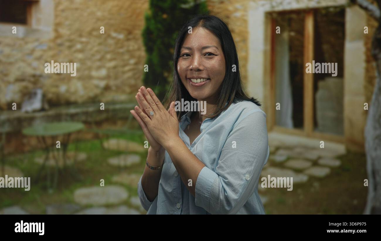Woman clapping hands at building entrance, smiling with visible ring on ...