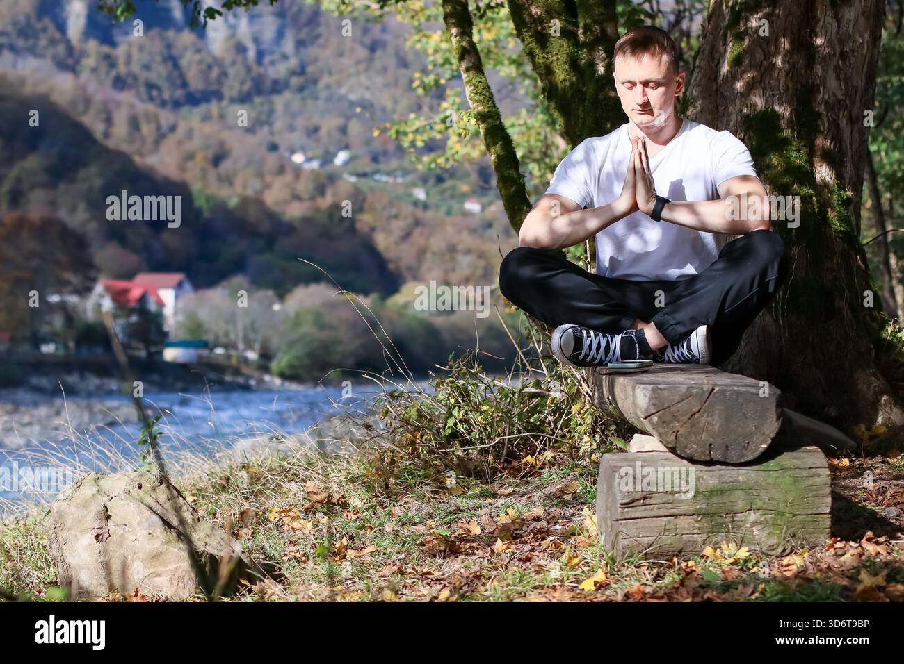 Male in casual attire meditates cross-legged on log near tree, hands ...
