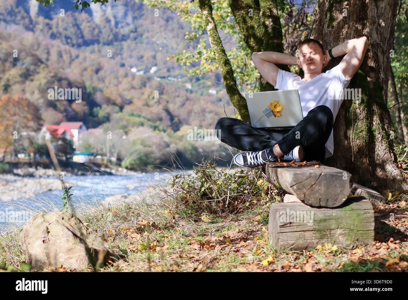 Young man in cross-legged pose relaxes with arms behind head and open ...