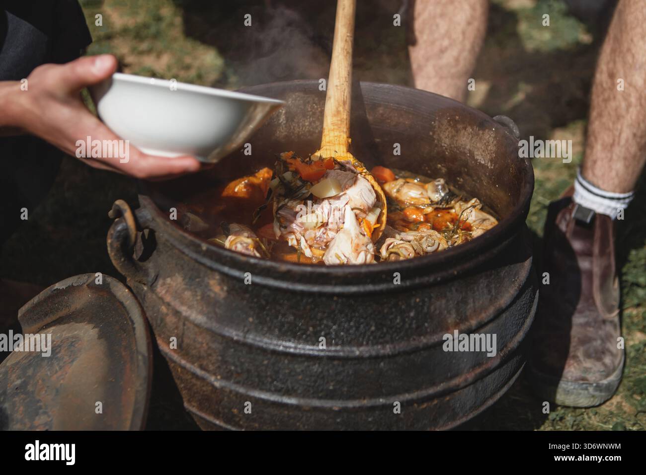 Traditional stew cooking outdoors in a cast iron cauldron. A person ...