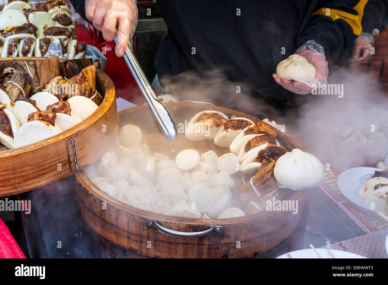 Close up of hand holding tongs removing a dumpling from a bamboo bowl ...