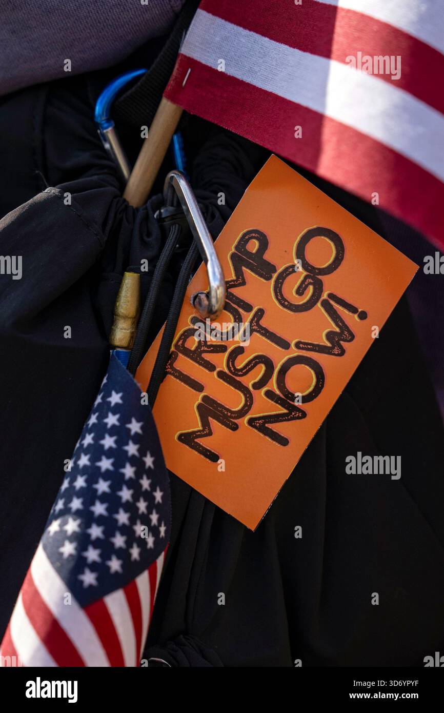 A woman's backpack has a "Trump Must Go Now" sticker surrounded by ...