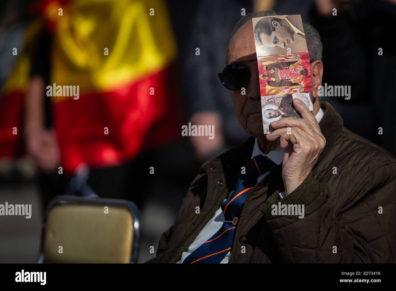 A man covers his face from the sun with a placard showing the images of ...
