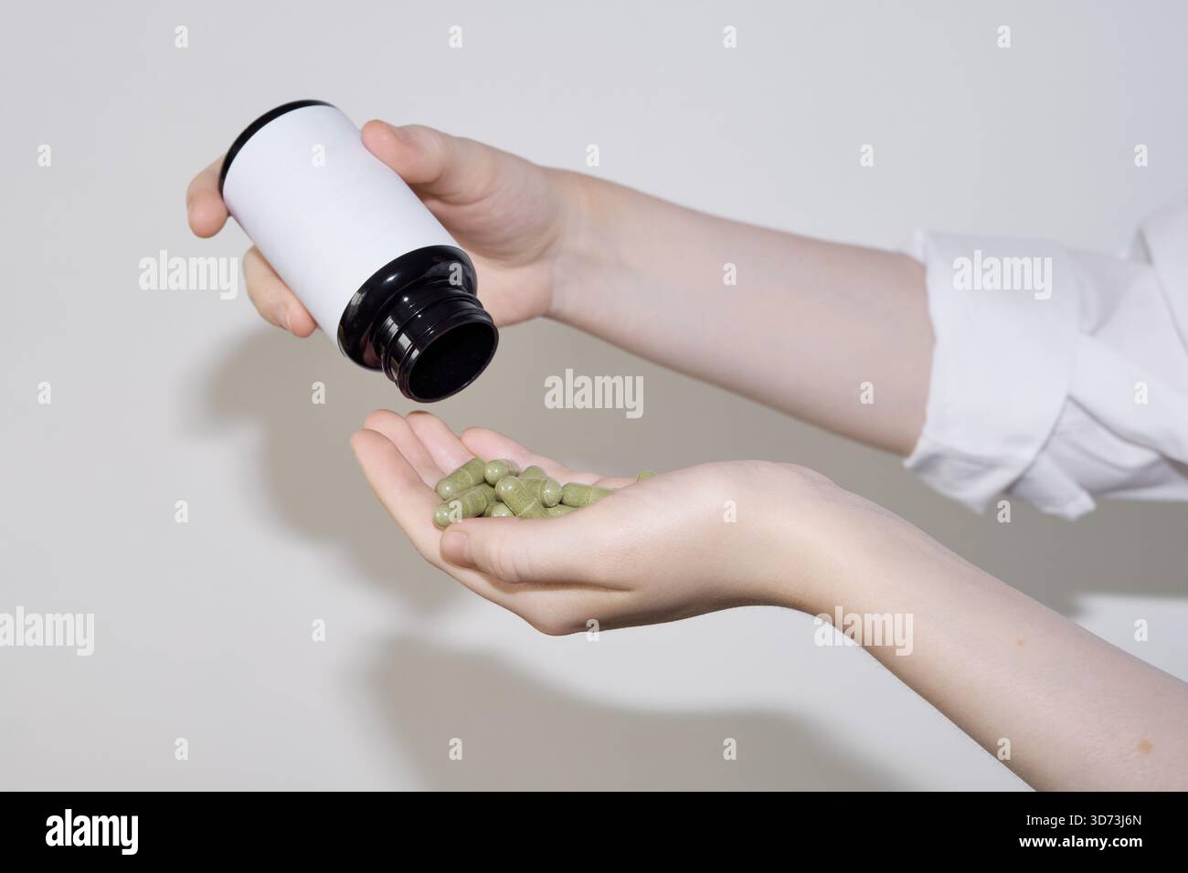 Female hand pouring green herbal capsules from bottle into her palm ...
