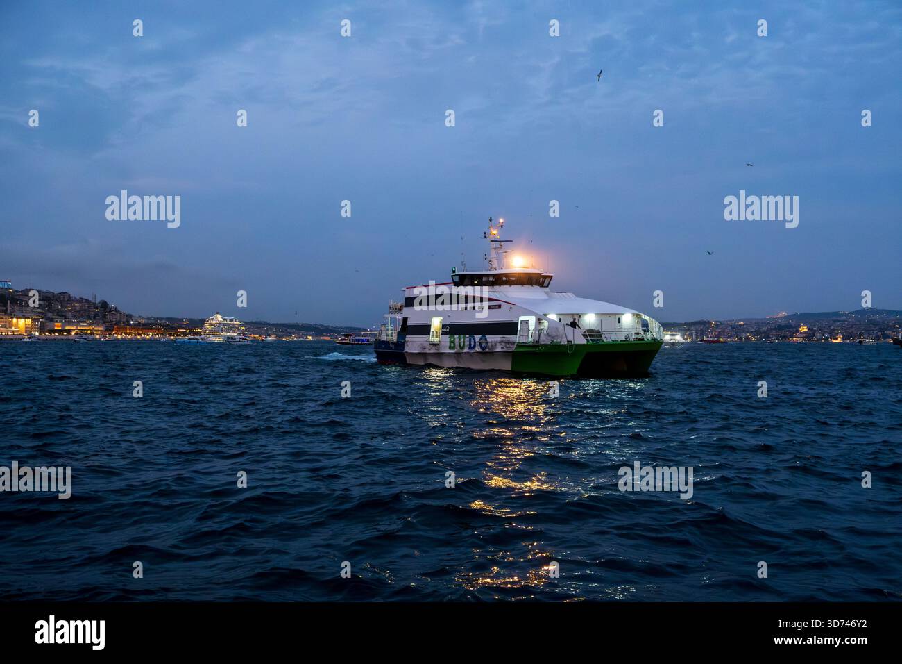Istanbul ferry with bright lights crossing Bosphorus Strait at dusk ...