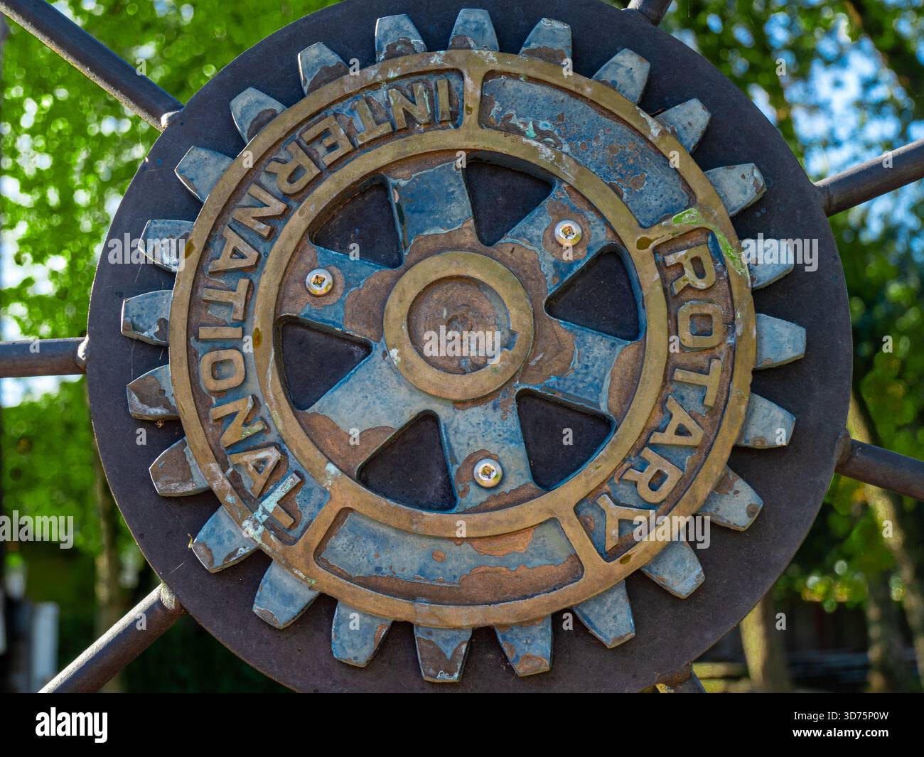 Weathered Rotary International gear emblem outdoors, sunlit metal with ...