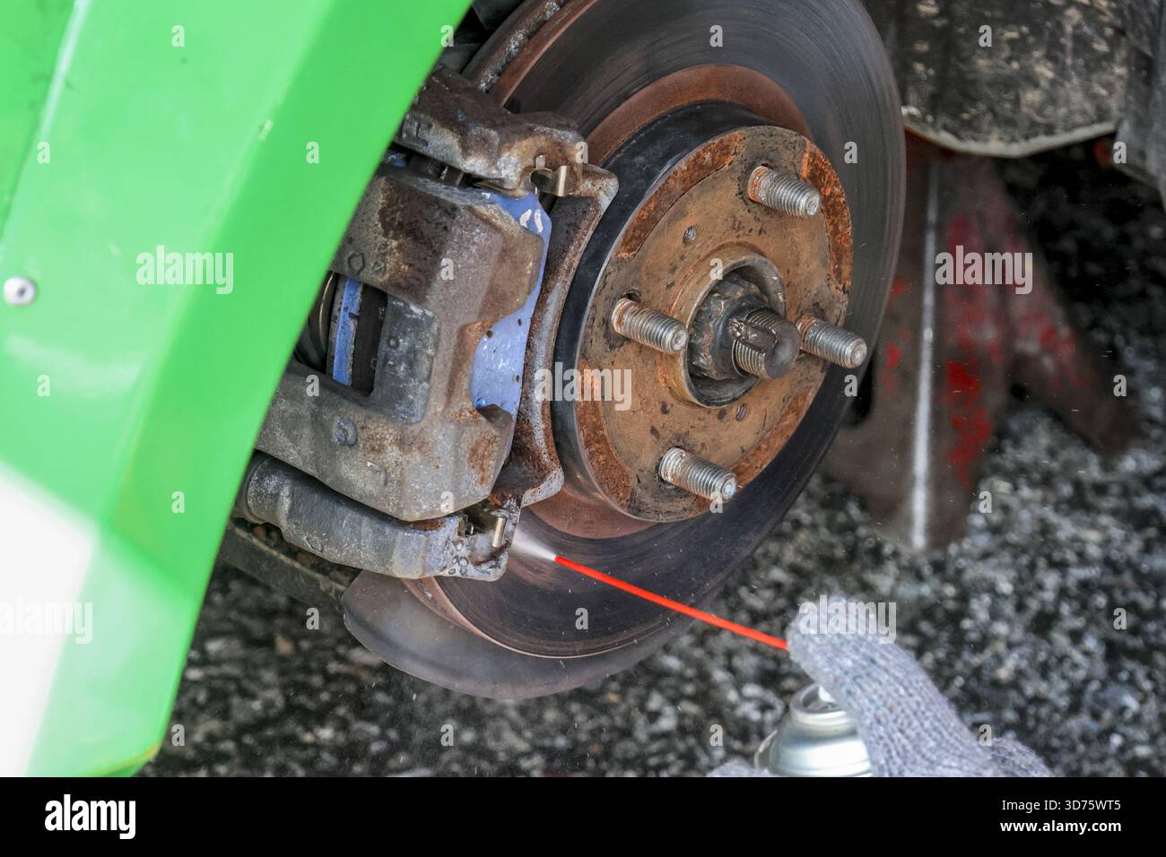 Mechanic performing car repair, spraying rusty brake rotor and caliper ...