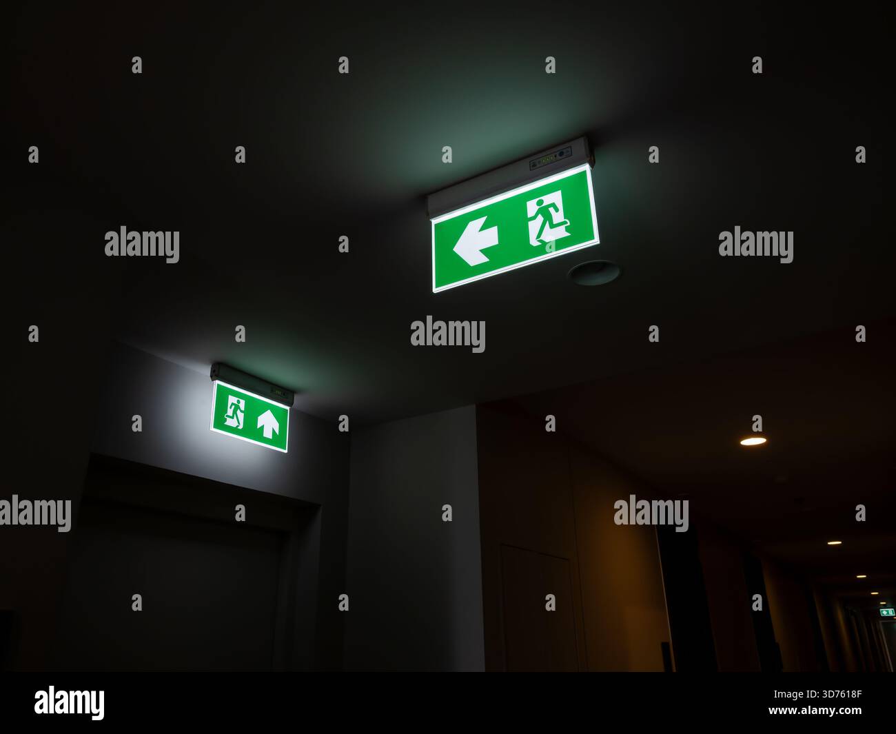 Green illuminated emergency exit signs in a dark hallway indicate ...
