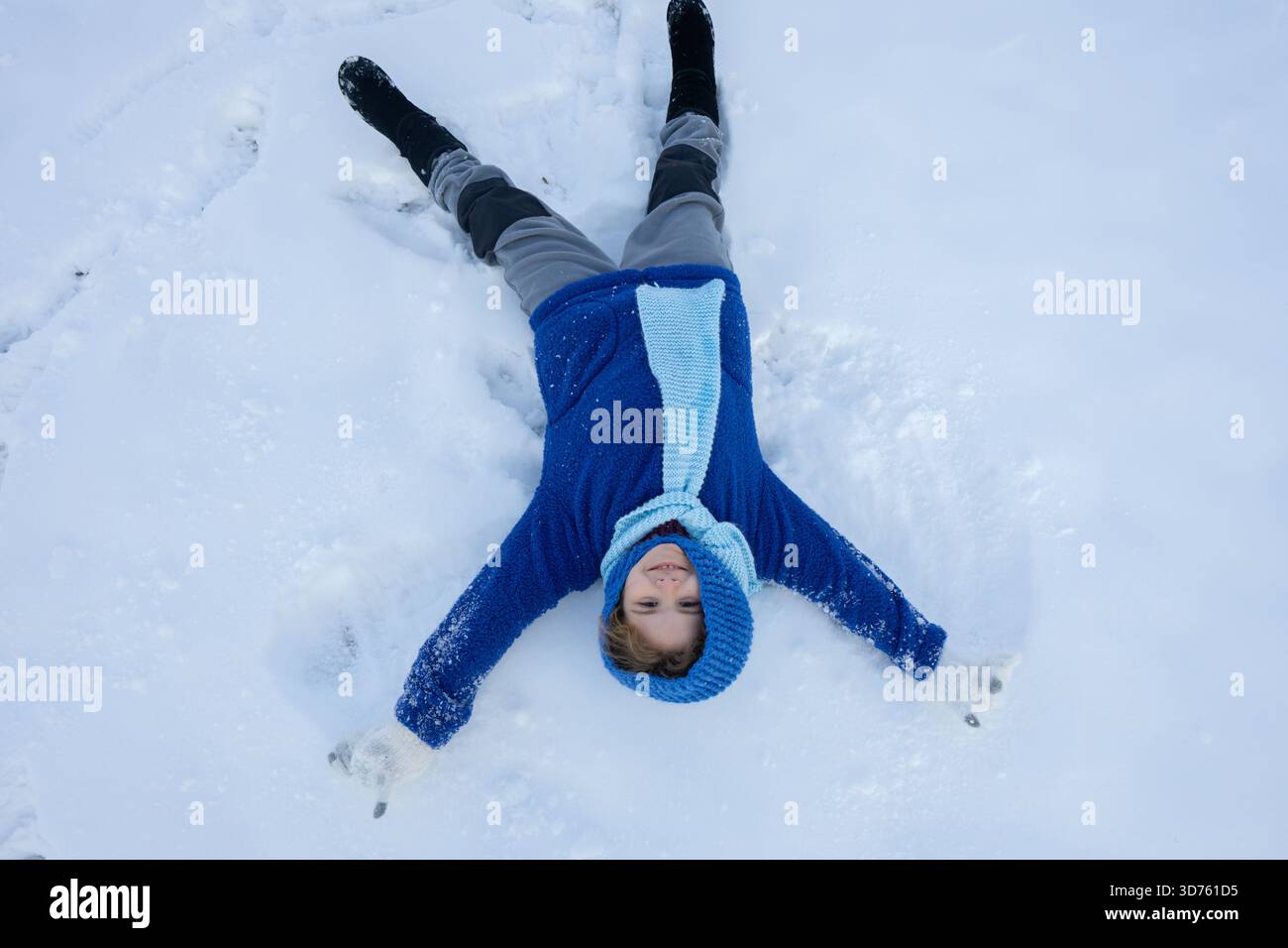 Child making a snow angel. Happy kid lying in the snow with snowy angel ...