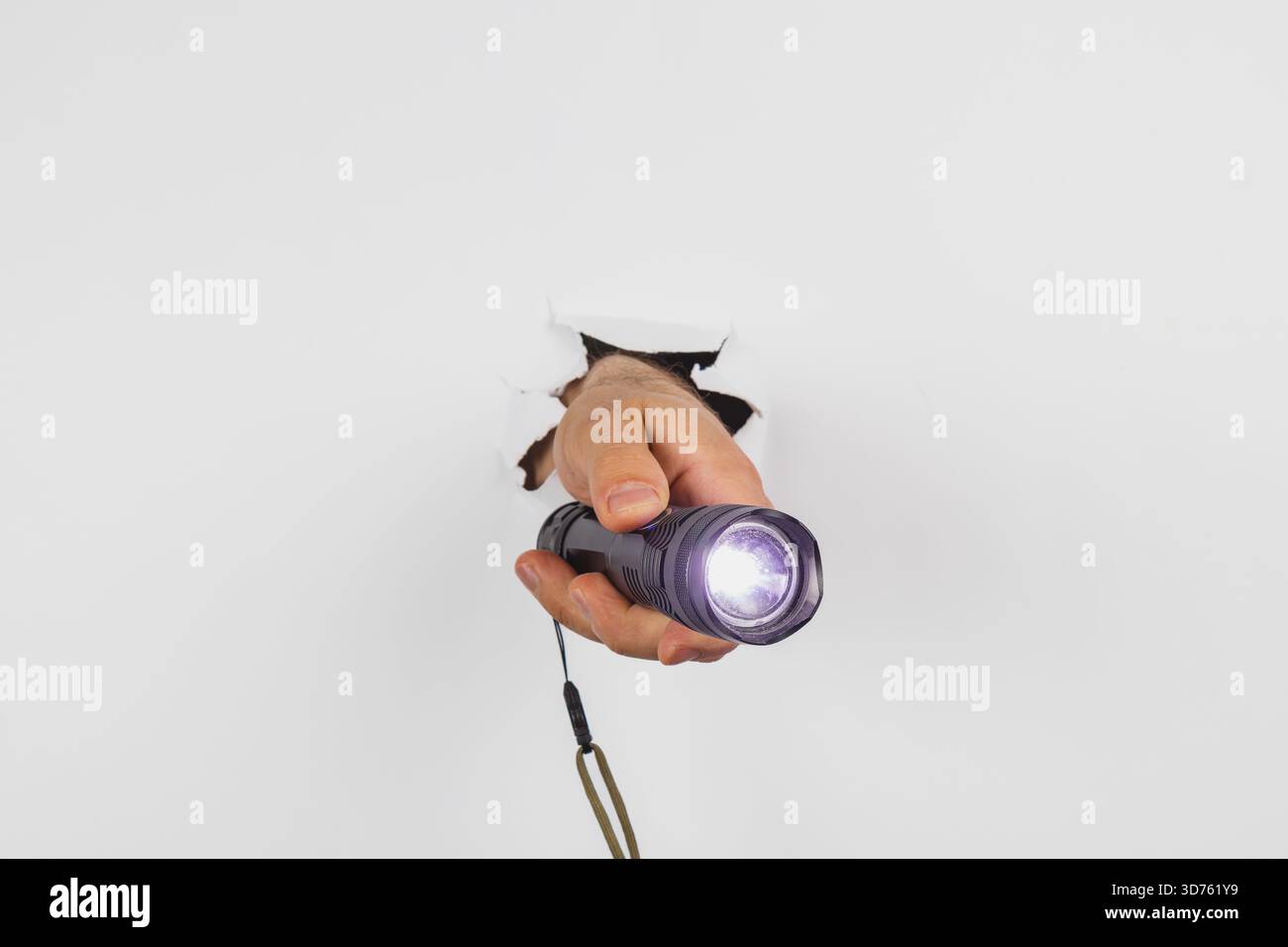 A hand holding a flashlight appears through a hole in a white wall ...