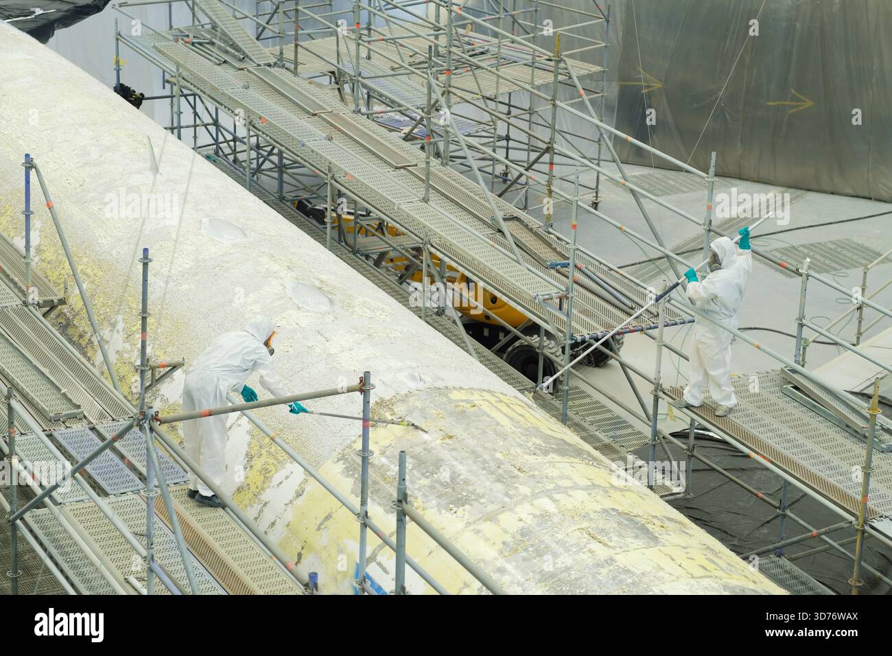 Two workers in protective suits clean a large aircraft wing supported ...