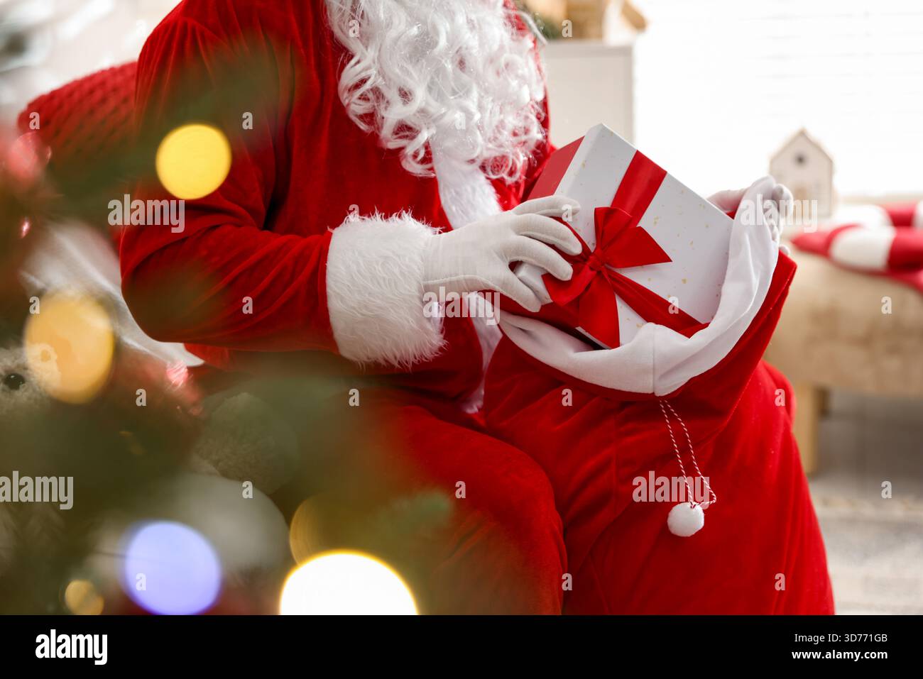 Santa Claus taking gift out of sack near Christmas tree at home ...