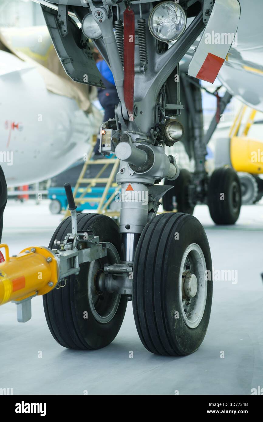 Technicians work on the landing gear of an aircraft inside a well-lit ...