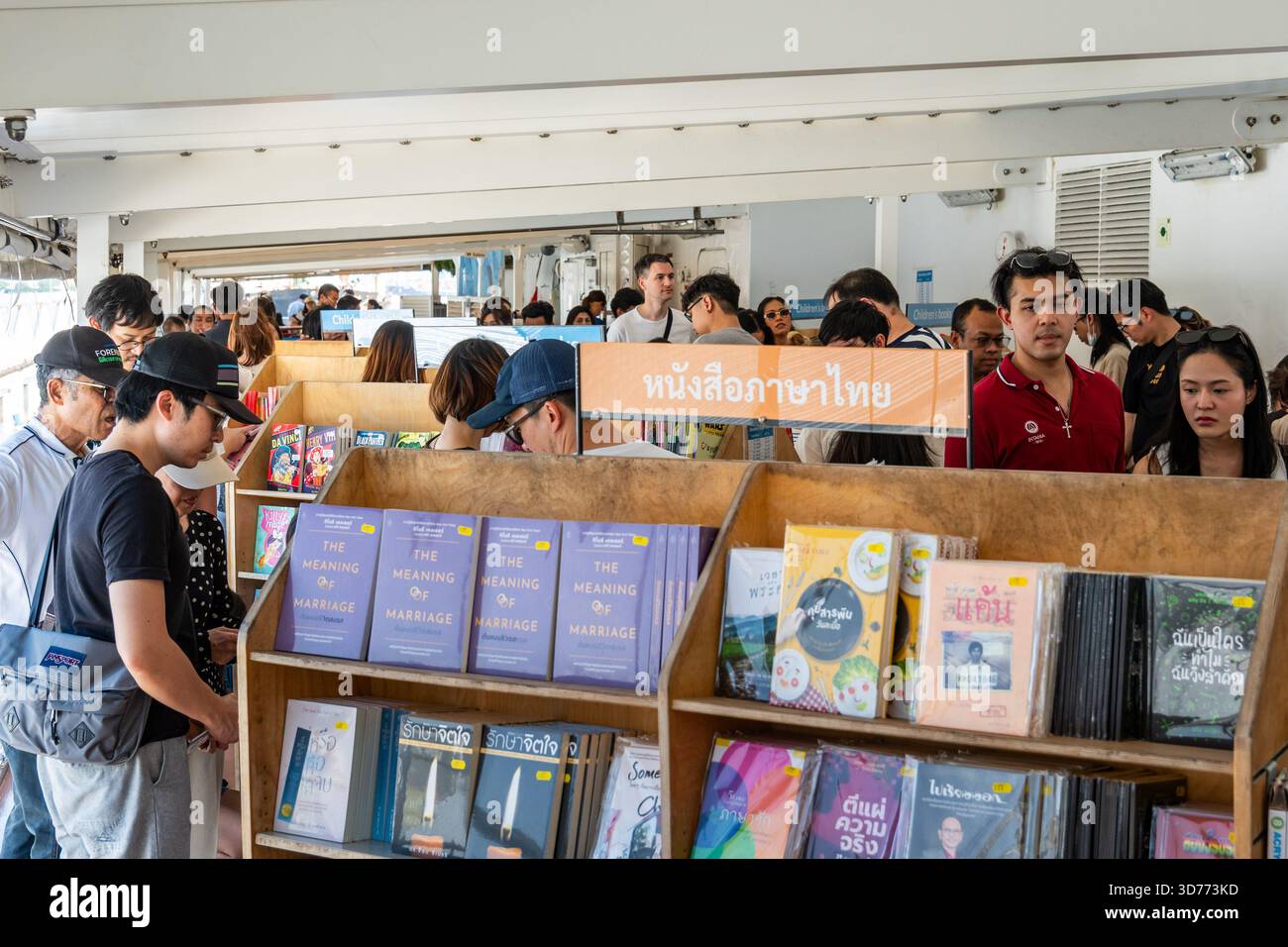 Visitors walk through the rows and shelves displaying books, mostly in ...